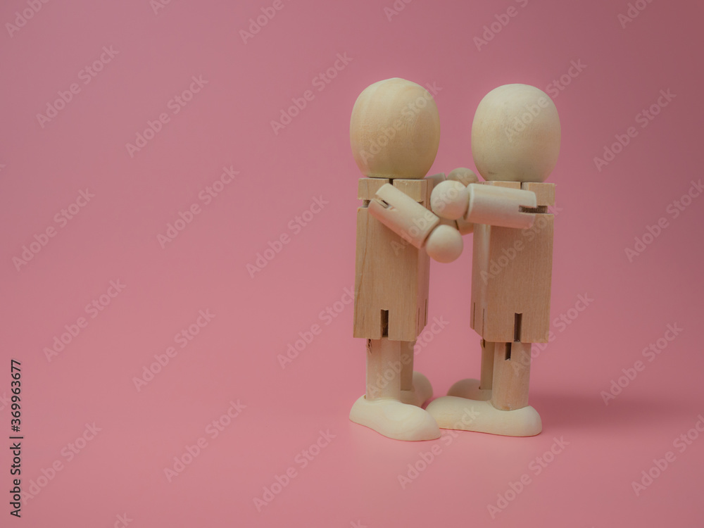 2 wooden dolls hugging each other on a pink background. Concept of ...