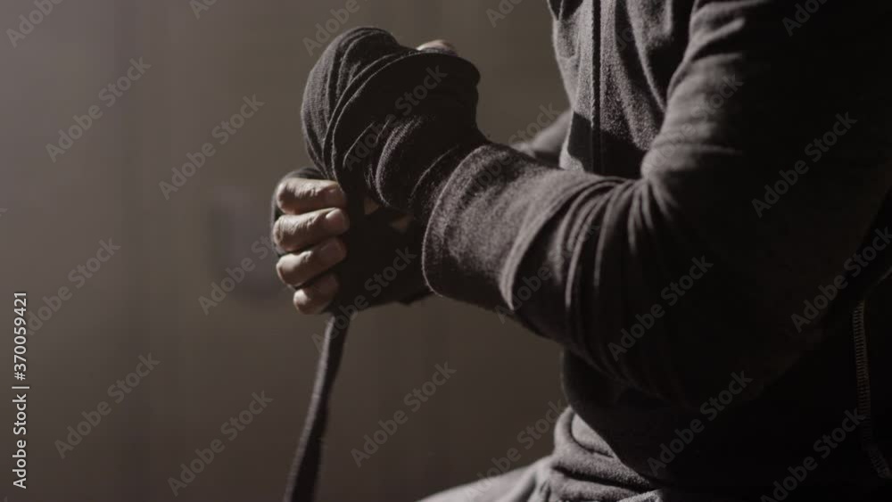 Boxer, Muay Thai fighter putting on hand wraps while sitting on a bench ...