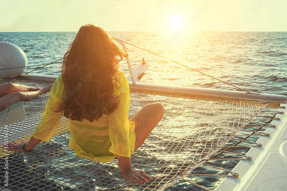 Woman sits on the deck of a sailing catamaran at sunset in the sun ...