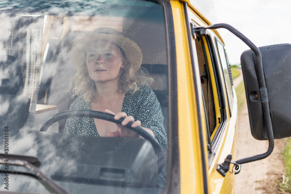Young blonde woman driving yellow camper van though the countryside ...