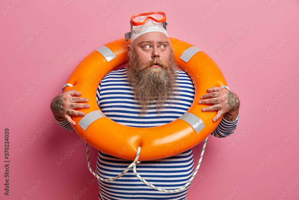 Serious bearded man with swimming hat and goggles, looks away, wears ...