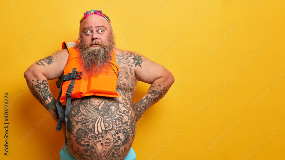 Plump shocked lifeguard poses with hands on waist, has stout tummy ...