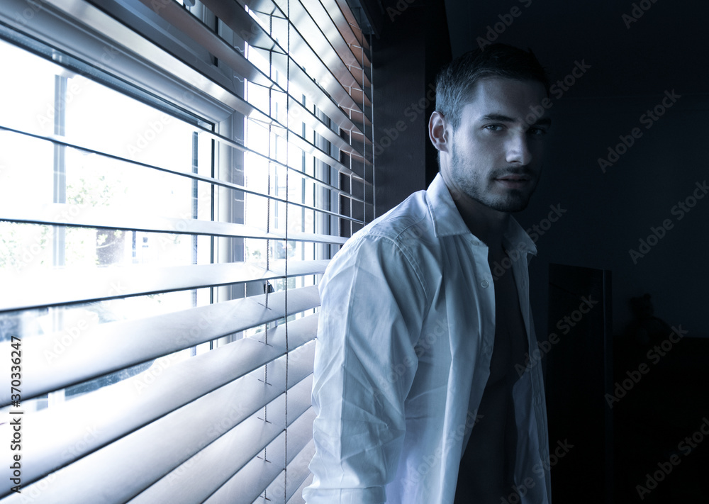 Portrait of handsome man with beard standing next to window with open ...