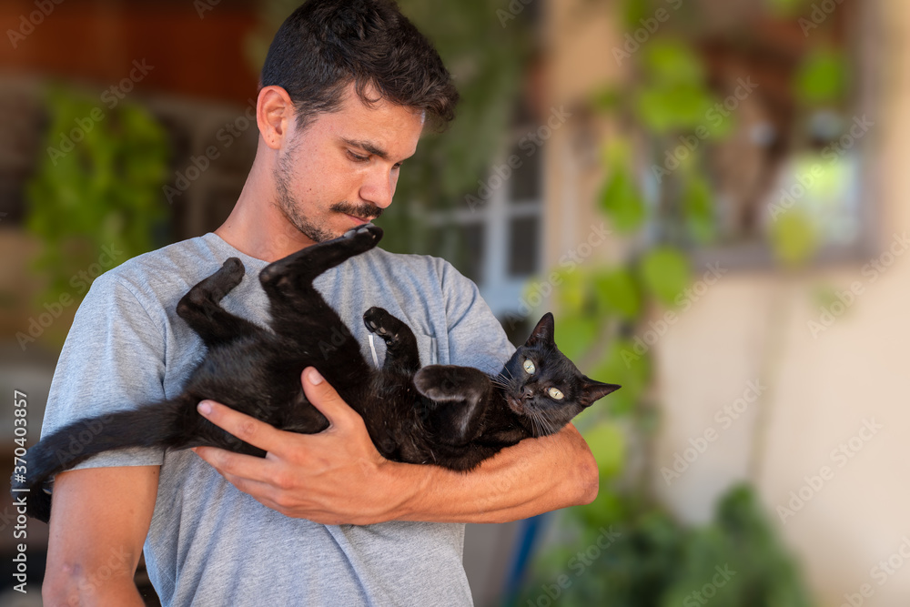 Hombre joven sostiene entre sus brazos a un gato negro con ojos verdes ...