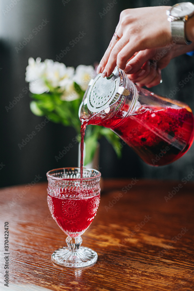 Cold red lemonade from a clear decanter is poured into a glass. Red ...