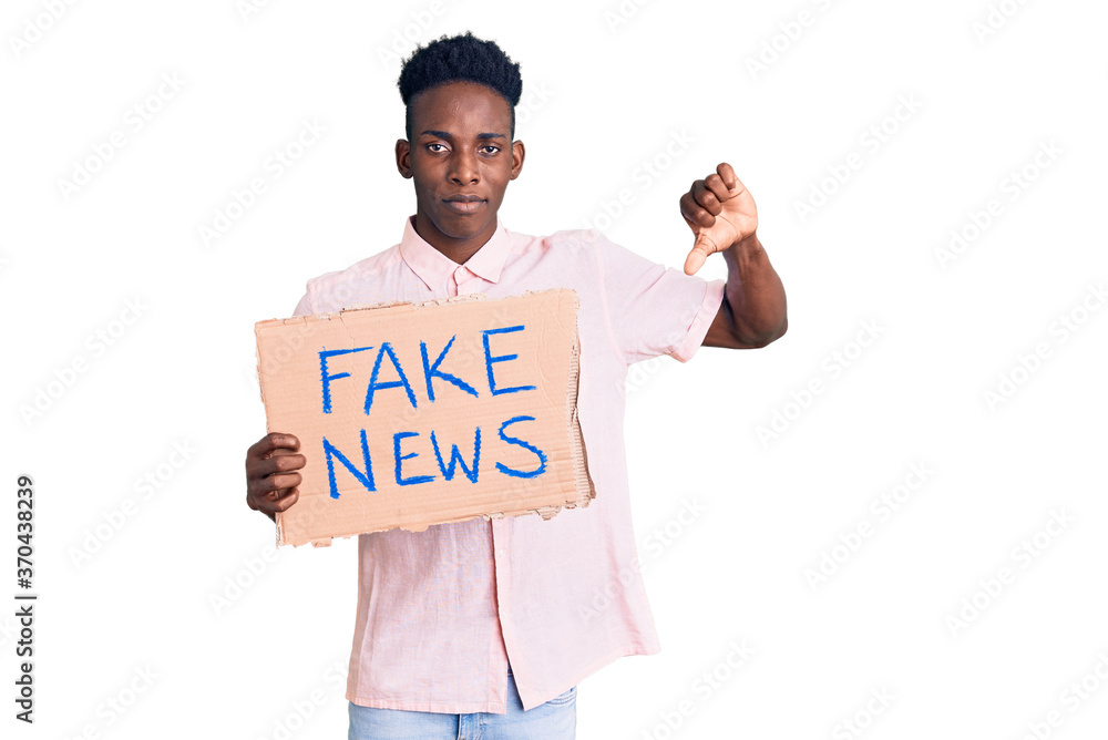 Young african american man holding fake news banner with angry face ...
