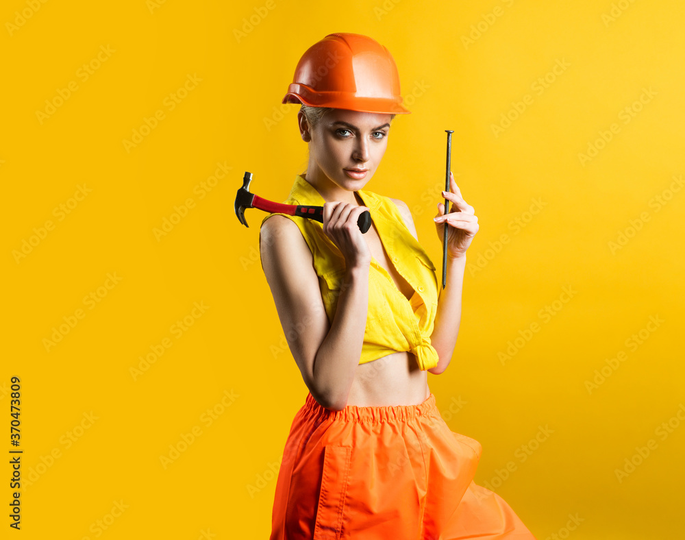 Sexy woman in helmet to use hammer. Young woman hammering nail at ...