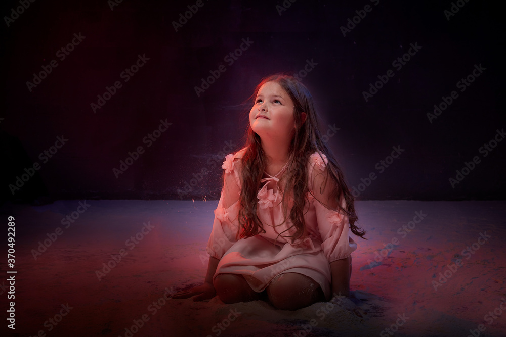 Small girl in white dress in dark studo during photoshoot with flour ...