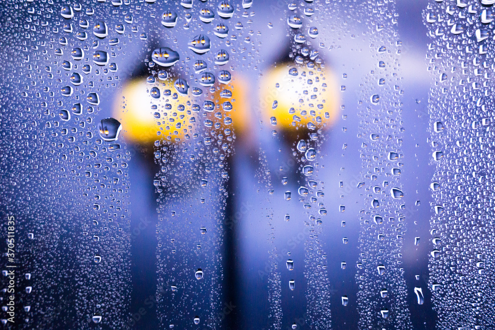 Rain water drops running on window glass lit by street lamps. Blurred ...