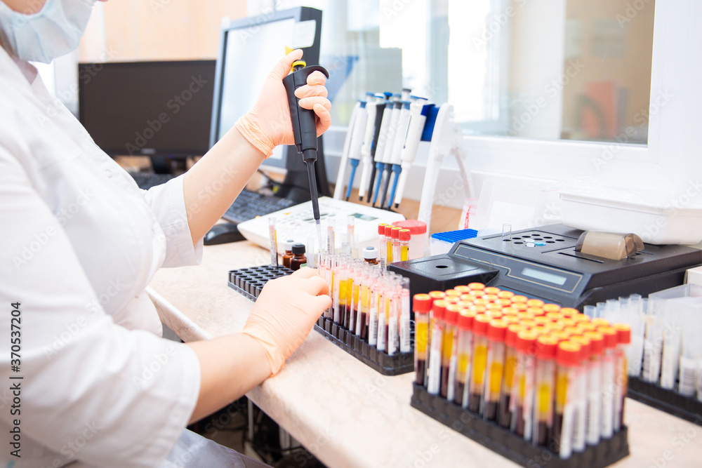 hands of a lab technician with a tube of blood sample and a rack with ...