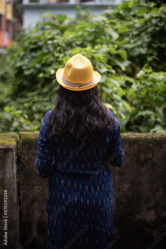 Backside view of an Indian woman standing in front of a green bush ...