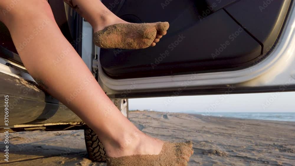Girl washing sand from her feet with clean water in a car on a beach ...