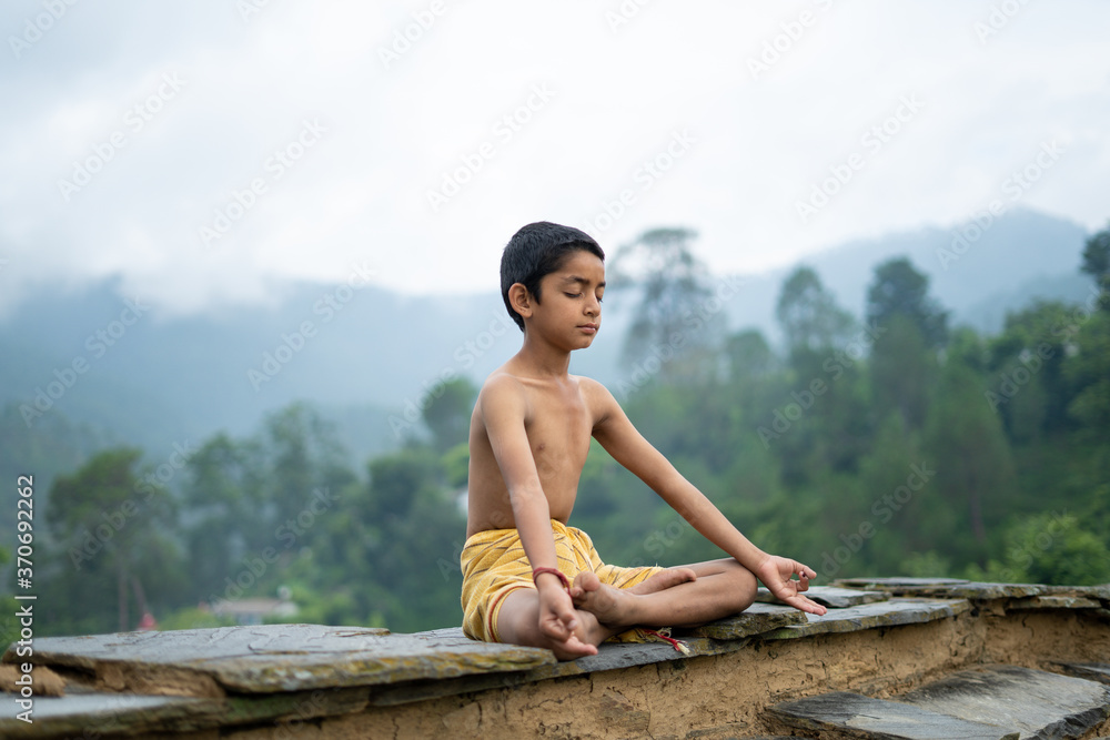 A young indian cute kid doing yoga in the mountains,wearing a dhoti ...