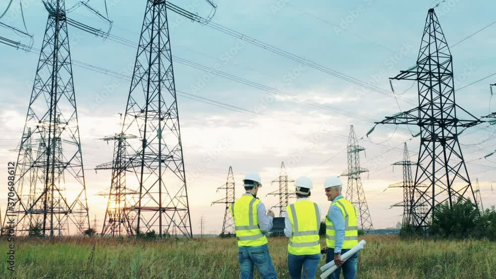 Power engineers are walking along the field with electrical towers ...
