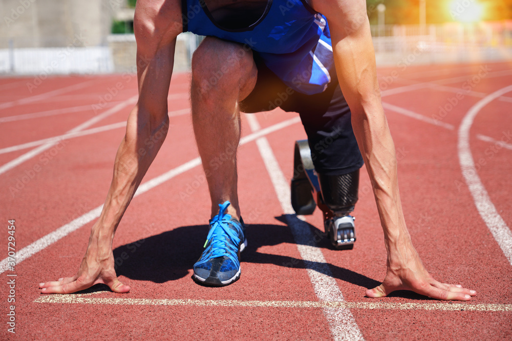 Adaptive sportsman with prosthetic foot at the start of running track ...