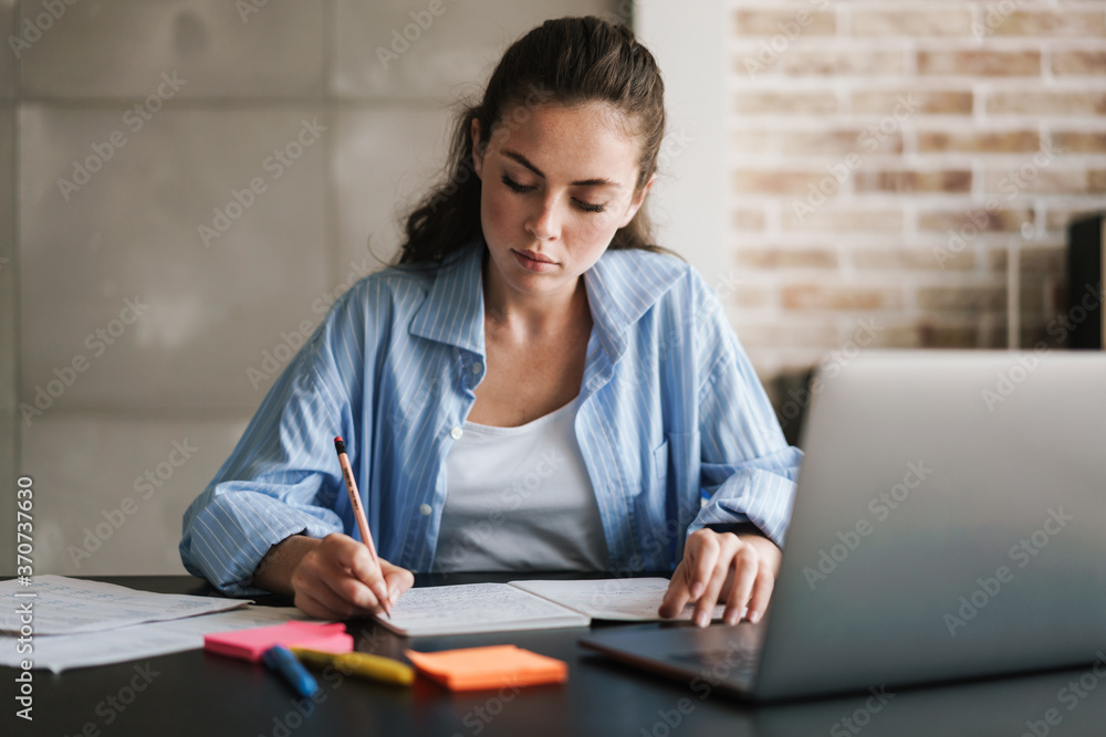 Concentrated girl using laptop computer while writing notes Stock Photo ...