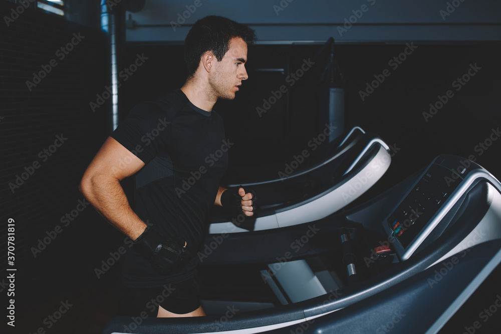 Fit man running in a gym on a treadmill looking to the screen ...