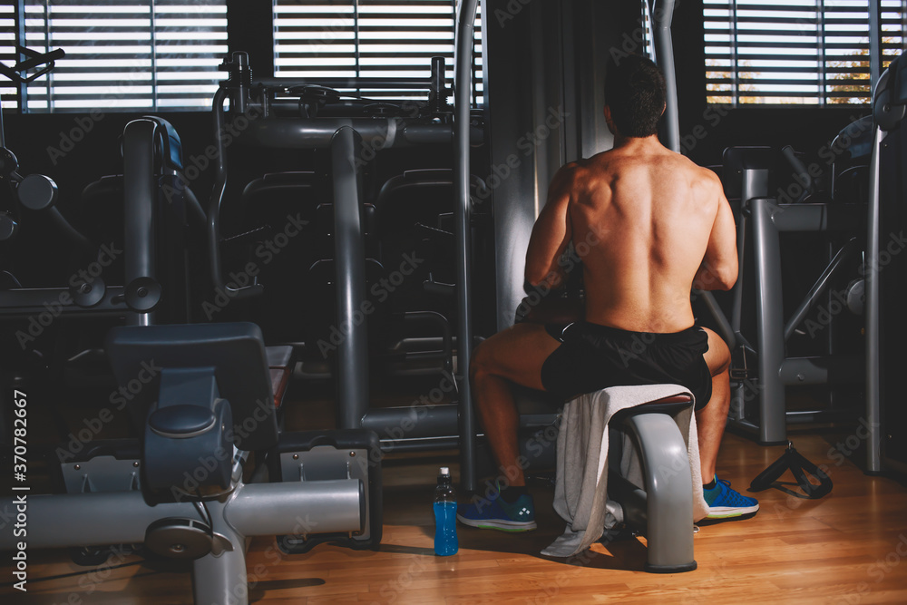 Athletic build sportsman working out arms' muscles on pulldown machine ...