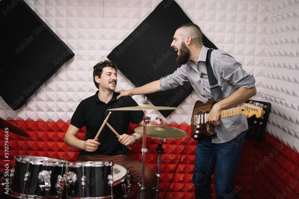Band members laughing while standing in music recording studio. Drummer ...