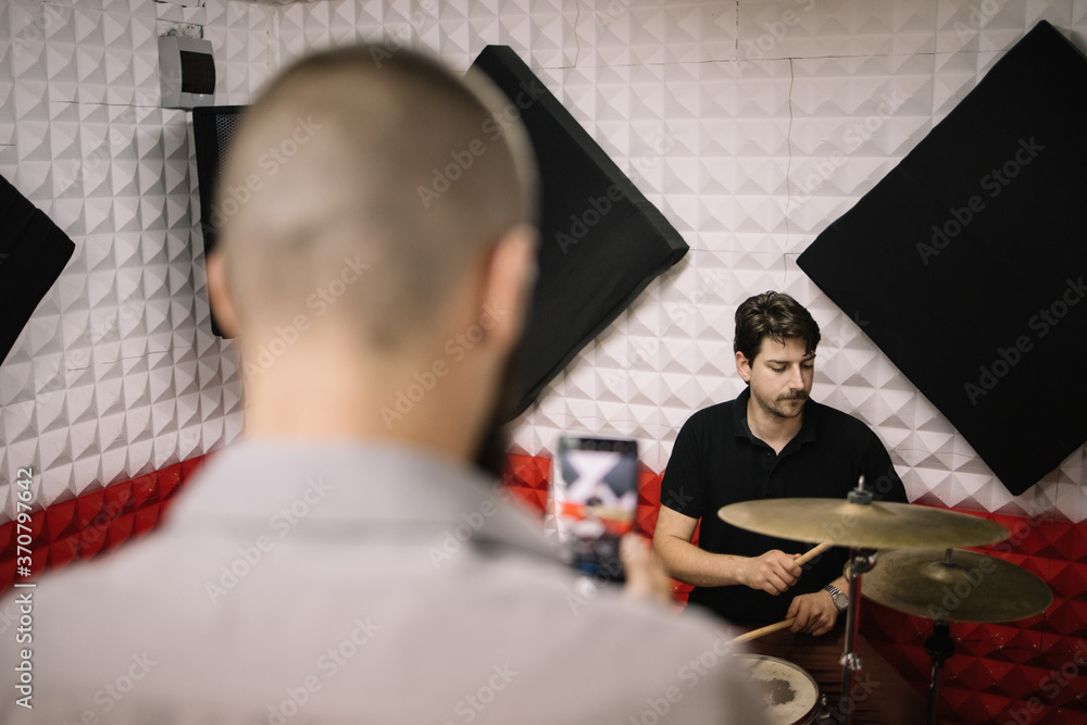 Blurred man taking photo of drummer sitting on drum set. Back view of ...