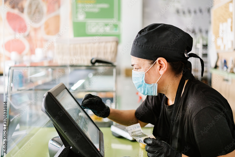 Side view serious female cashier wearing gloves and mask tapping on ...