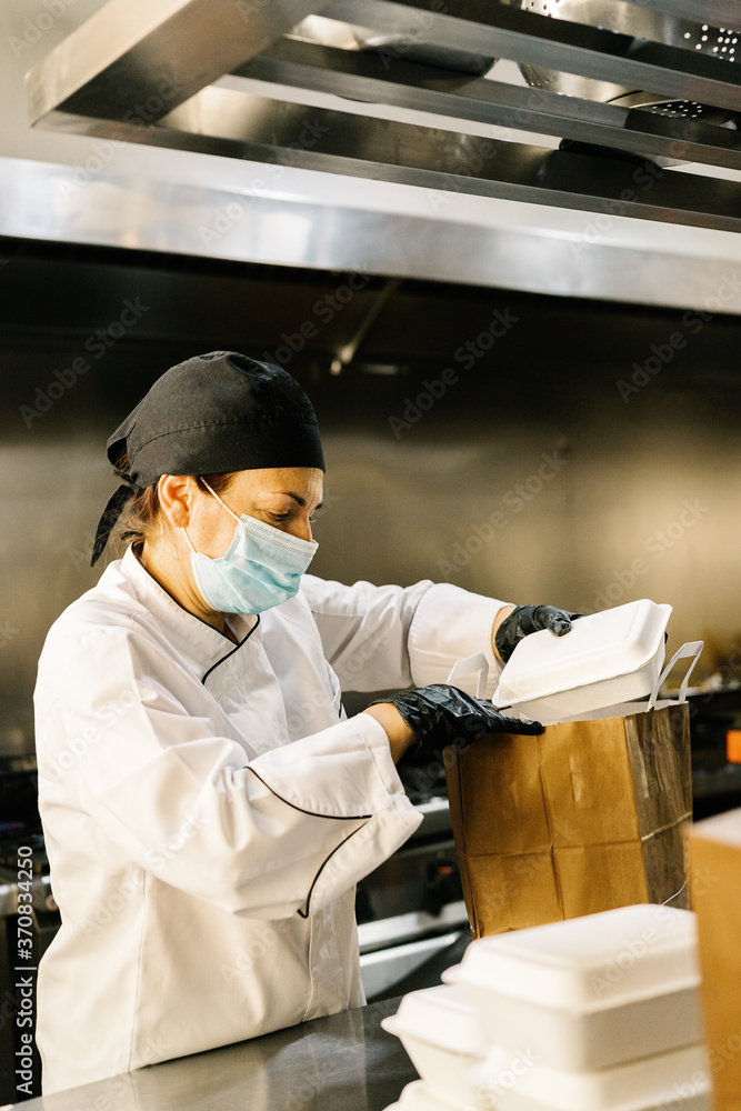 Concentrated female chef wearing face mask and uniform while working in ...
