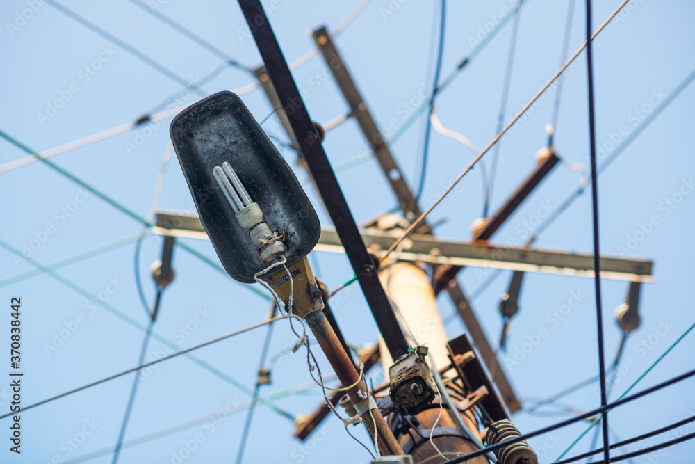 From below of street lamp hanging on electricity pole with many cables ...