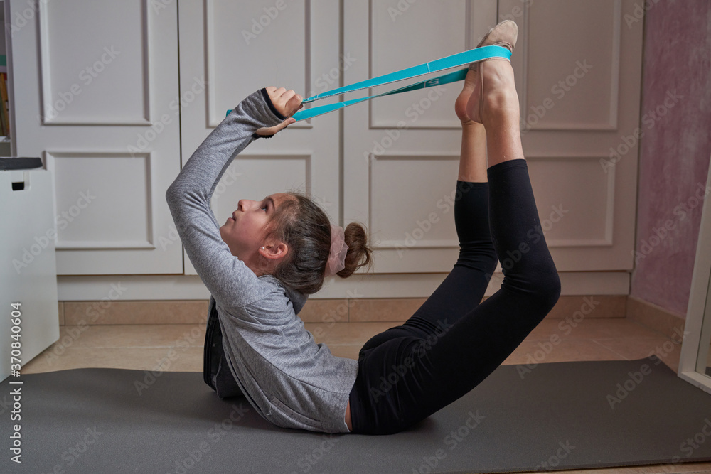 Side view of girl doing bow pose with elastic band while stretching ...