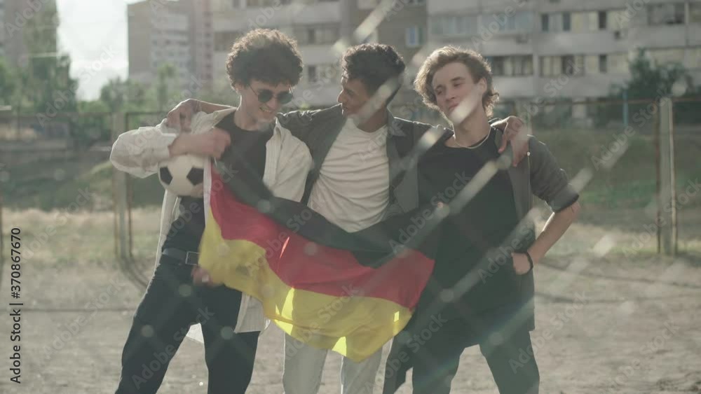 Three happy multiethnic friends posing with sport ball and German flag ...