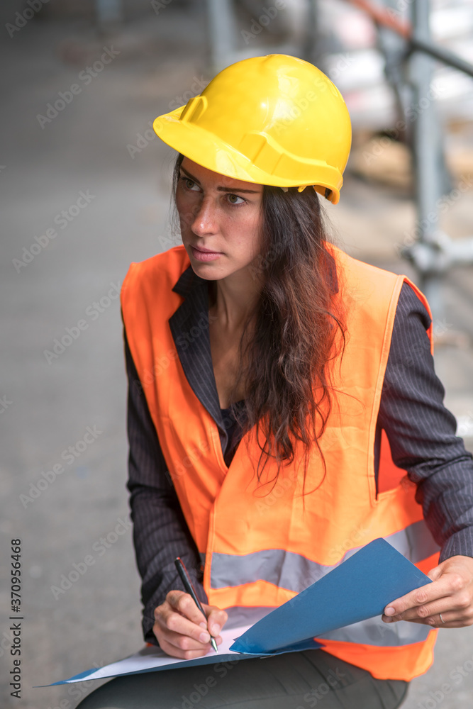 Absorbed female civile engineer wearing safety helmet and vest checking ...