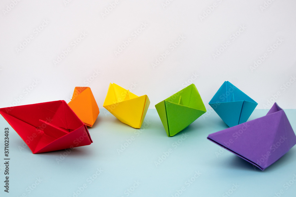 Colored paper boats with the colors of the rainbow on a light blue ...