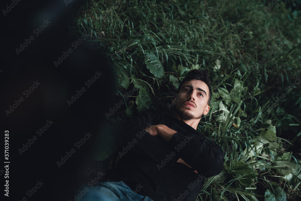 Handsome man in the forest stretches his feet to a tree and lies on the ...