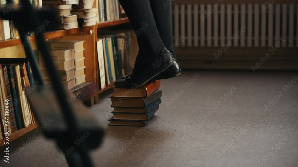 Legs of girl that stands on the books trying to reach upper shelves in ...