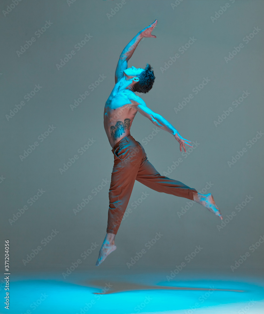 Cool young guy dancing and floating in the air in a jump in neon light ...
