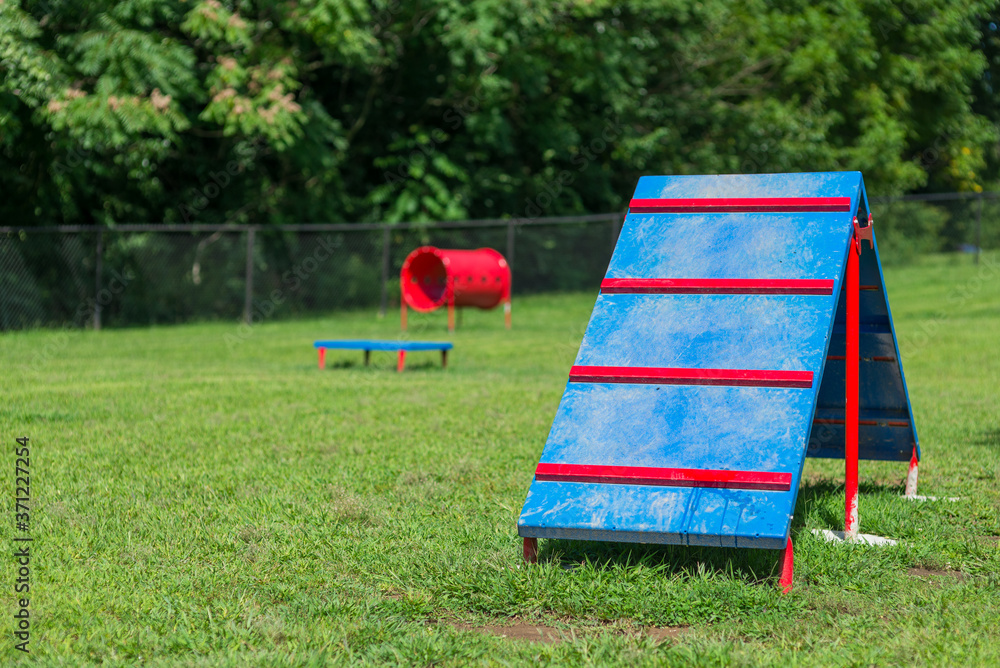 Dog agility equipment at a fenced in dog park. A-frame ramp with steps ...