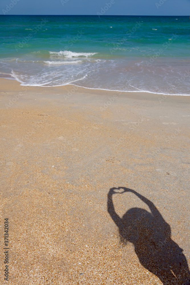 Shadow of girl making a heart shape with her hands, standing on a beach ...