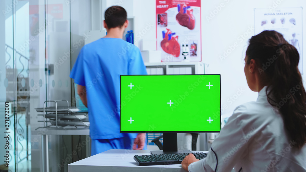 Physician using computer with chroma key and assistant holding patient ...
