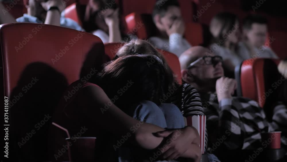 Close-up of frightened teenage girls watching scary movie in cinema ...
