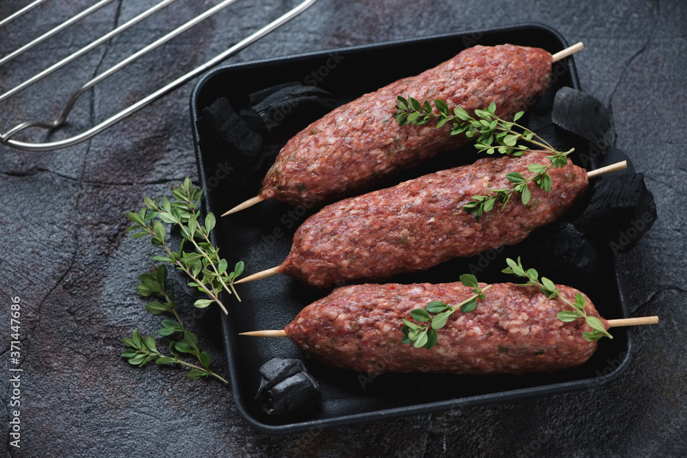 Cast-iron tray with raw seasoned beef lula kebabs and charcoals ...