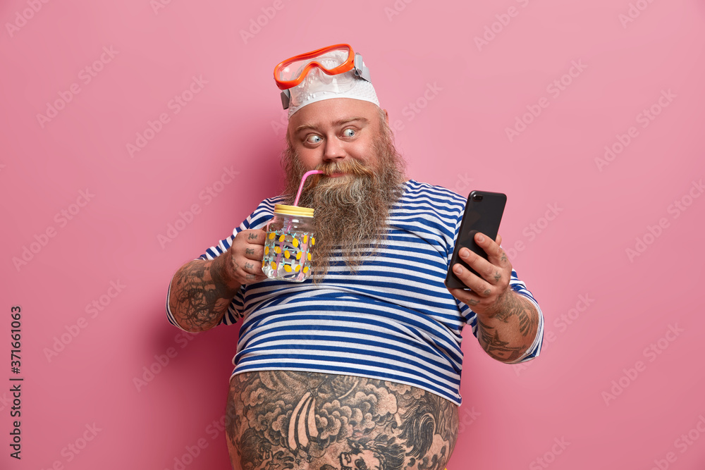 Positive fatso guy drinks fresh water, takes photo via cellphone, wears ...