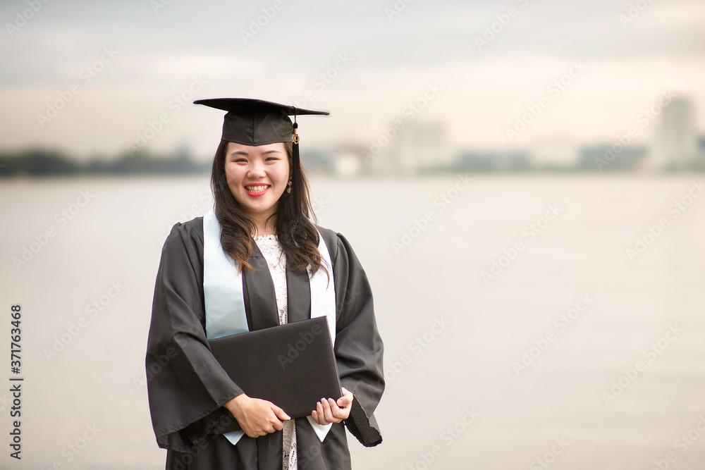 Happy Asian student holding degree certificate file while wearing gown ...