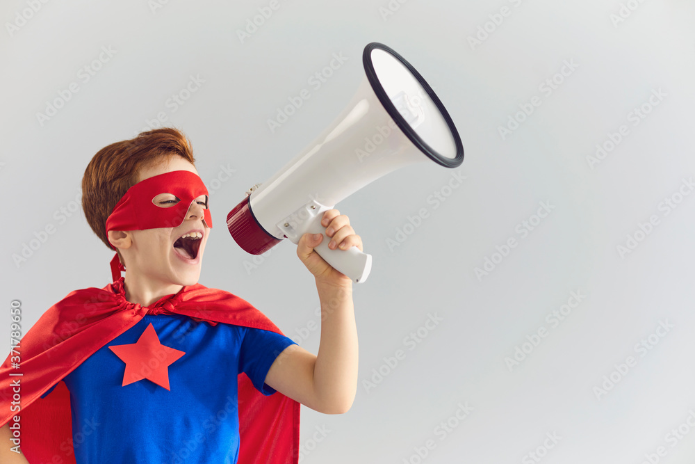 Cute boy dressed as superhero shouting into megaphone on grey ...