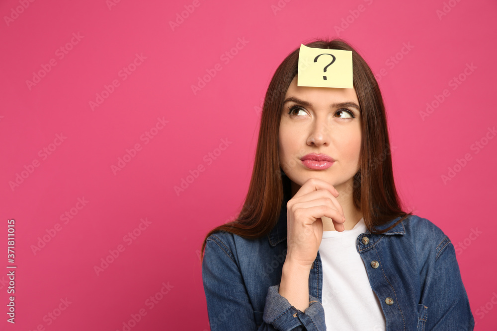 Pensive woman with question mark sticker on forehead against pink ...