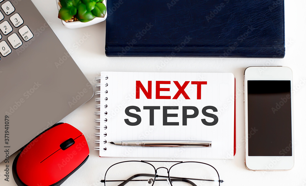 Laptop, pen and notepad with text NEXT STEPS in the white background ...