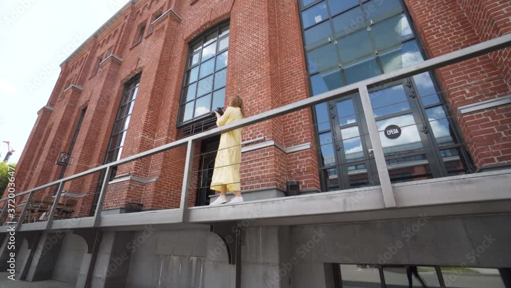 Beautiful woman takes photos with camera from balcony of office brick ...