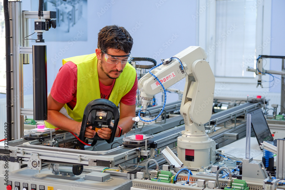 Man is programming robot arm with control panel which is integrated on smart factory production ...