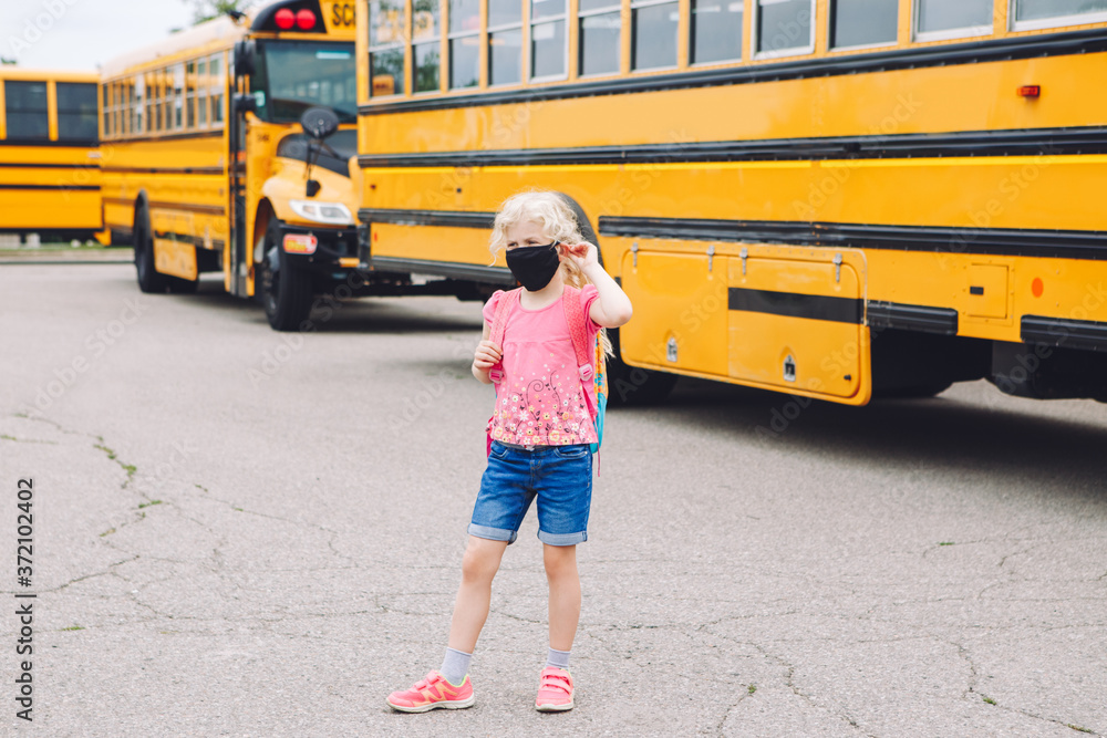 Happy Caucasian girl student wearing face mask near yellow bus. Kid ...