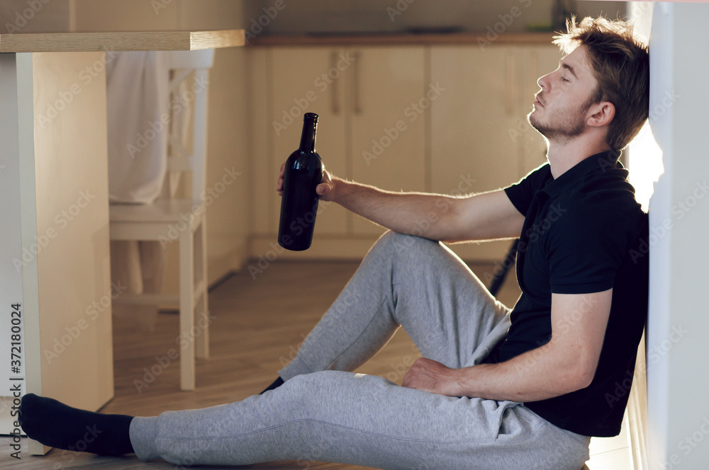 Side view, drunk young man with bottle of wine sitting on the floor in ...