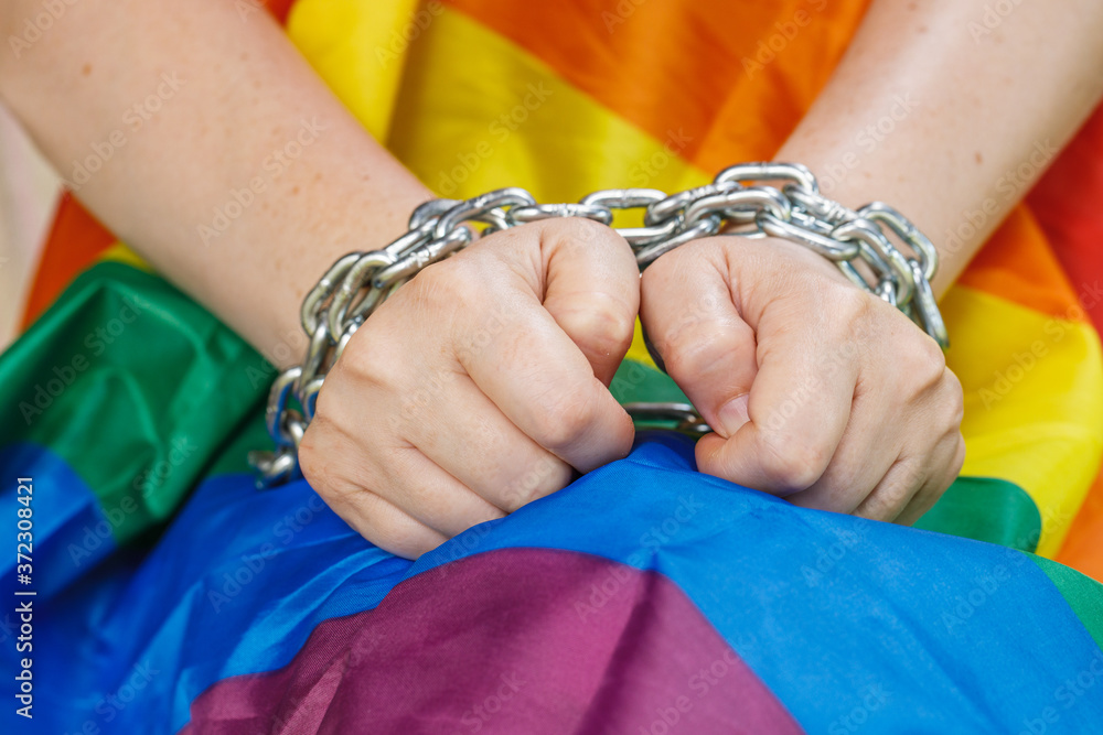 Female hands chained against the background of the LGBT flag. The ...