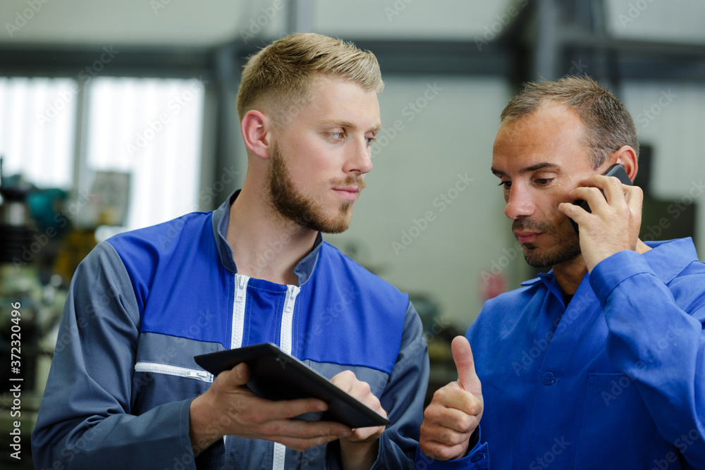 mechanic using a phone while colleague shows him tablet Stock Photo ...